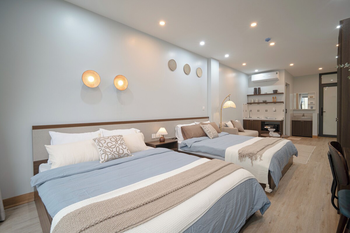Quarto de hotel com duas camas, uma mesa, uma cadeira, um espelho e um banheiro visível através de uma porta aberta.