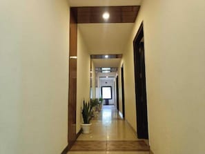Um corredor com piso ladrilhado, plantas em vasos e uma porta no final.