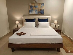 Cama bem arrumada com lençóis brancos, dois travesseiros e uma pequena bandeja no lado esquerdo.