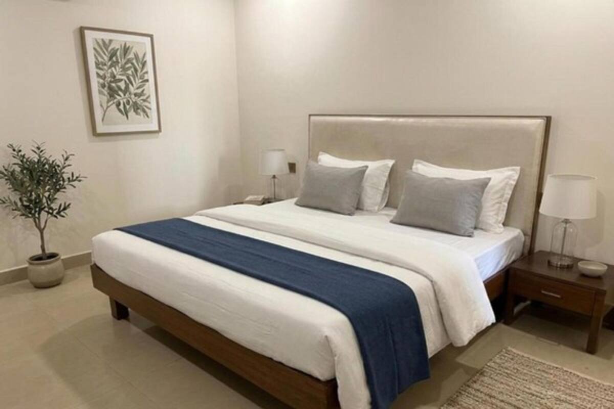 Quarto com cama, mesas de cabeceira, luminária, planta e um quadro na parede.