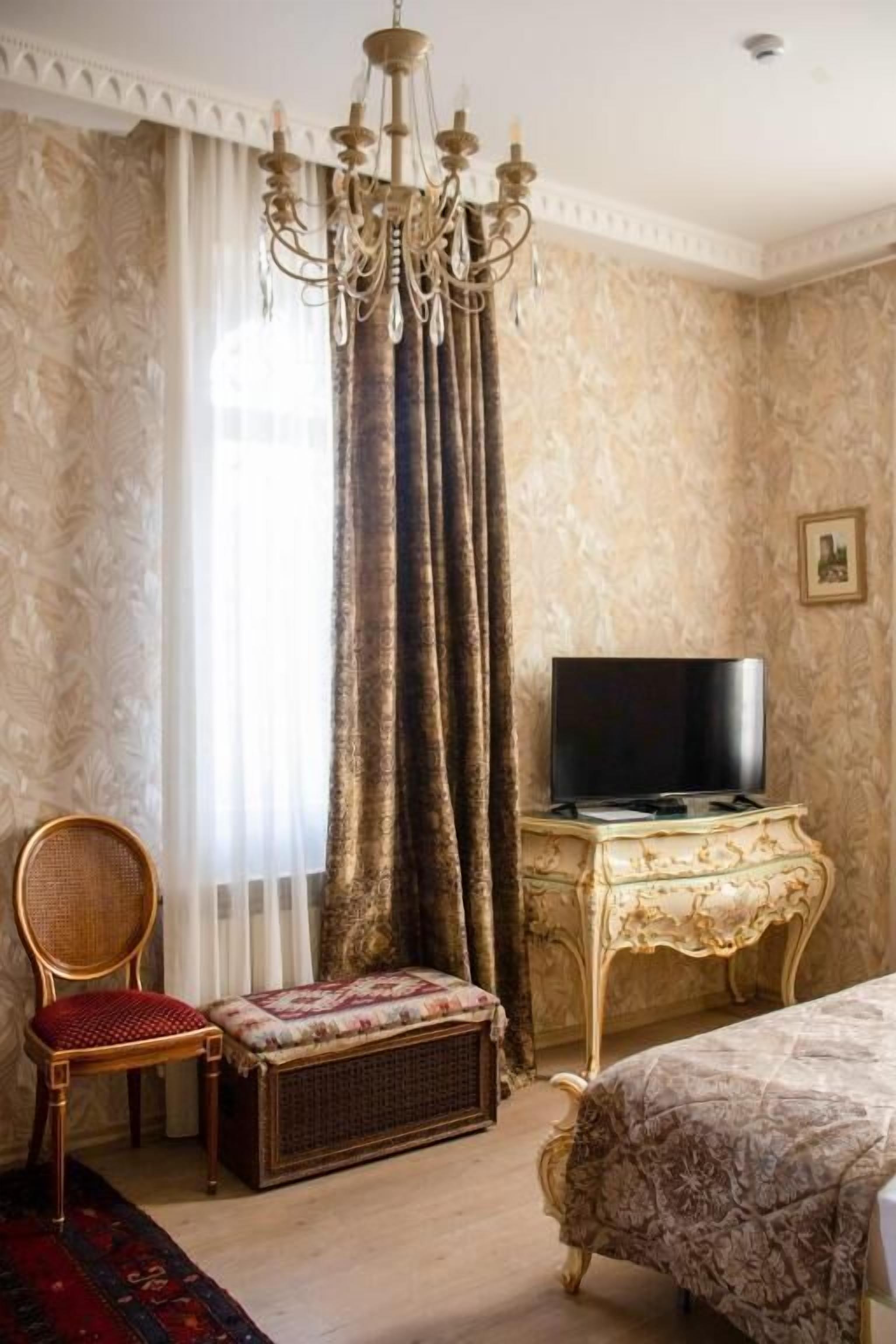 Um quarto com uma cama, televisão sobre um suporte, uma cadeira, um banco e um candelabro.