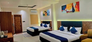 Quarto de hotel com duas camas, um guarda-roupa de madeira, uma escrivaninha com cadeira e obras de arte nas paredes.