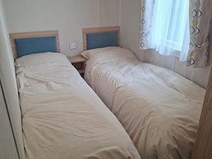 Quarto duplo com duas camas, uma mesa de cabeceira e uma janela com cortinas.