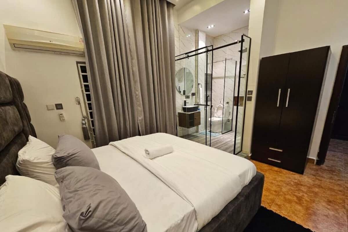 Quarto moderno com uma cama grande, divisória de chuveiro em vidro e um guarda-roupa.