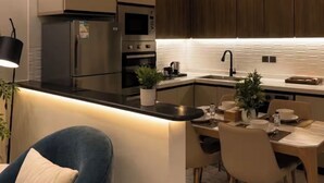 Cozinha moderna com eletrodomésticos embutidos, área de jantar com mesa e cadeiras, e uma poltrona azul.