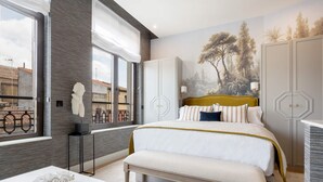 Quarto moderno com uma cama grande, um banco, uma mesa branca e vista para o exterior.