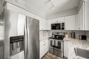 Uma cozinha moderna com eletrodomésticos de aço inoxidável, bancada de granito e armários brancos.
