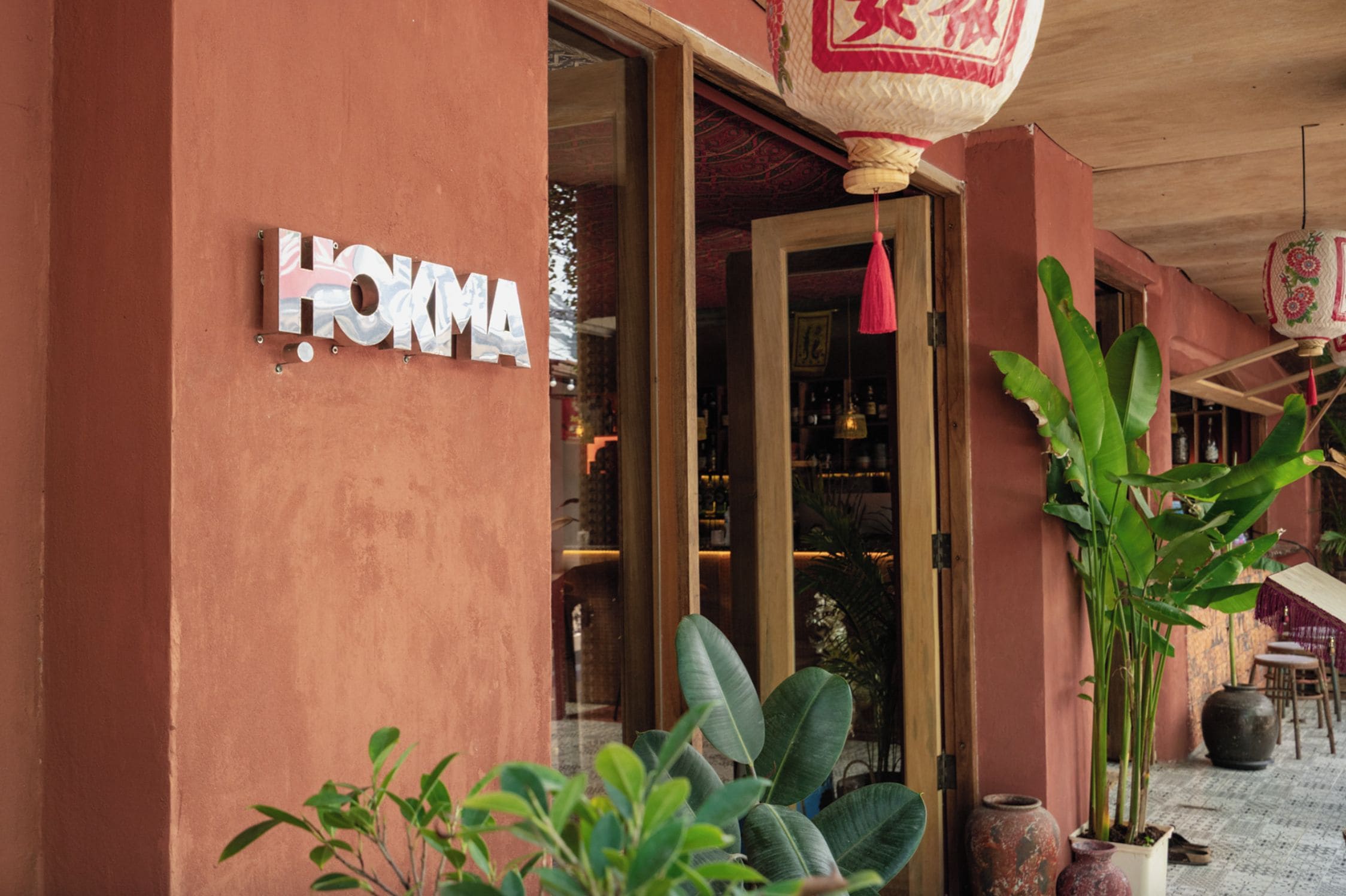 Entrada de um edifício com uma placa indicando 'HOWMA' e um tradicional candeeiro suspenso.
