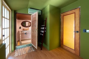 Um corredor com piso de madeira, parede verde e uma porta de madeira, além de uma janela.