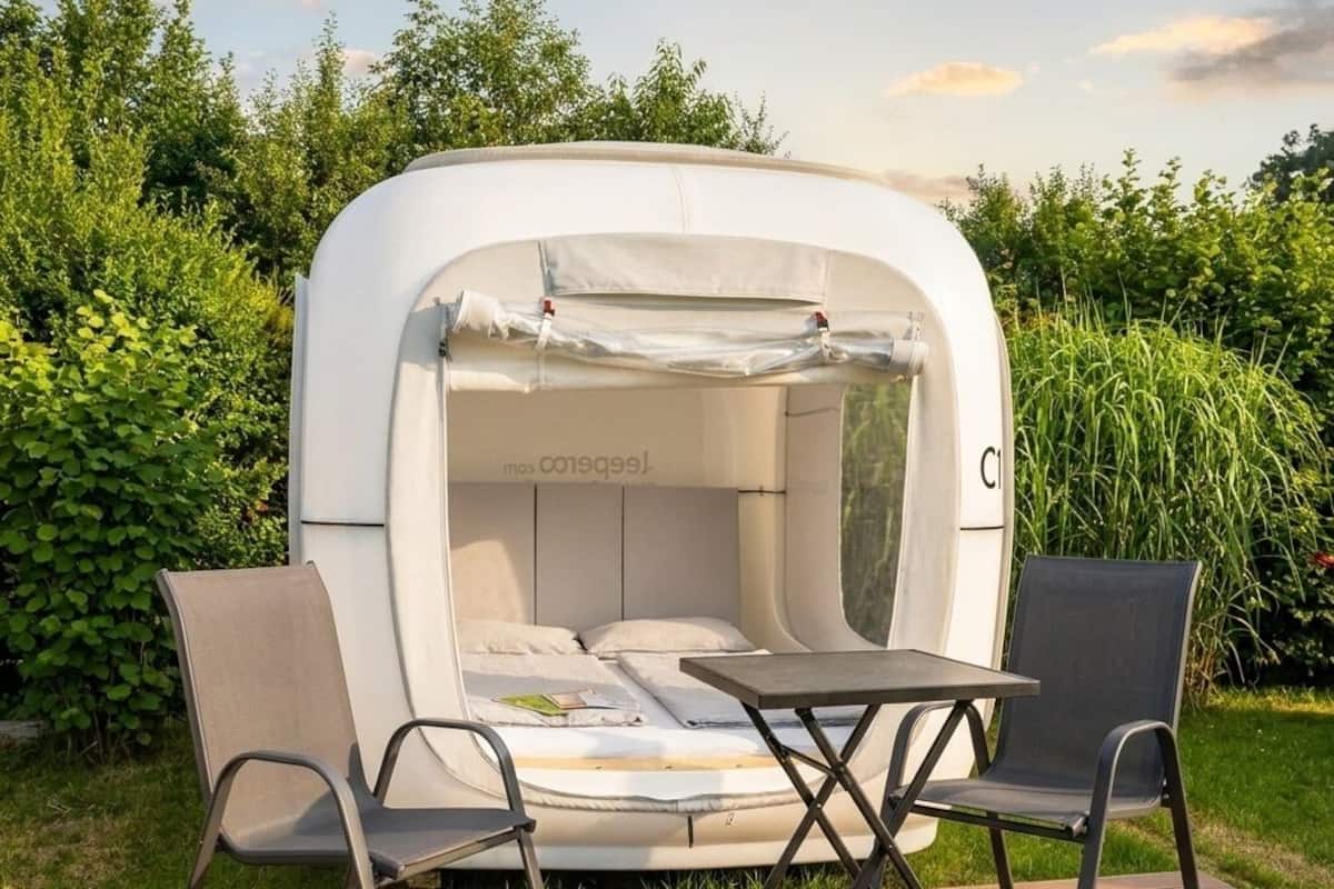 Uma cápsula de camping portátil com uma mesa e duas cadeiras, rodeada por vegetação.