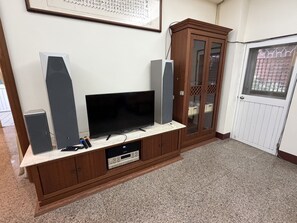 Sala de estar com televisão de tela plana, dois alto-falantes, controle remoto e um armário.
