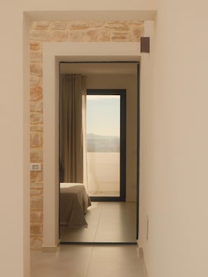 Quarto com parede de pedra, cama, janela com cortinas e vista do céu.