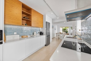 Uma cozinha moderna com armários brancos, geladeira de aço inoxidável, forno embutido e painel de azulejos.