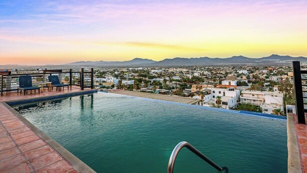 Uma piscina infinita com vista para a cidade, área de piscina com cadeiras e céu claro.