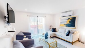 Uma sala de estar moderna com uma televisão de tela plana, um sofá, uma mesa de centro e um quadro na parede.