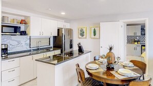 Cozinha moderna com armários brancos, uma ilha central e uma área de jantar com mesa e cadeiras redondas.