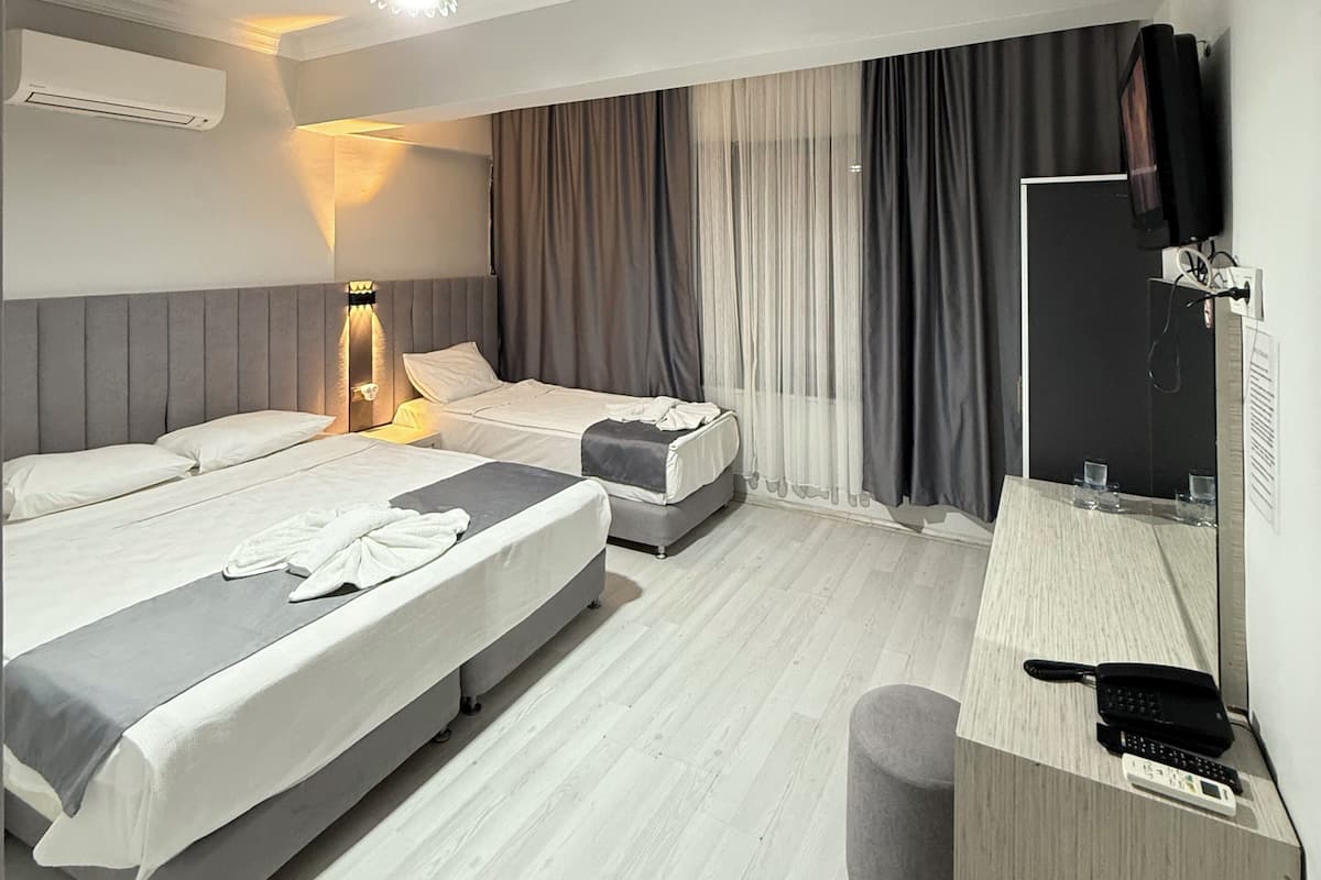 Quarto de hotel moderno com uma cama grande, mesas de cabeceira, uma escrivaninha com cadeira, um espelho e um aparelho de ar condicionado.