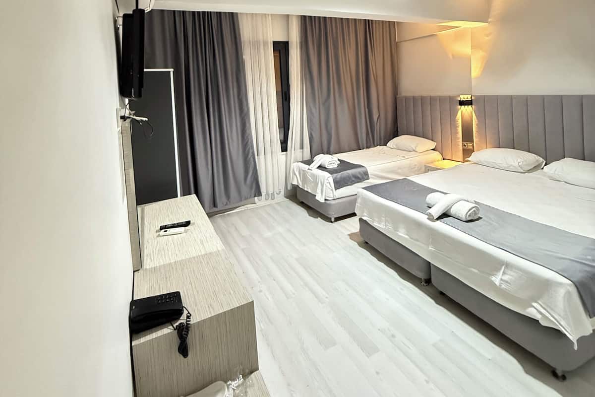 Quarto de hotel com cama, mesas de cabeceira, escrivaninha e telefone, e uma televisão.