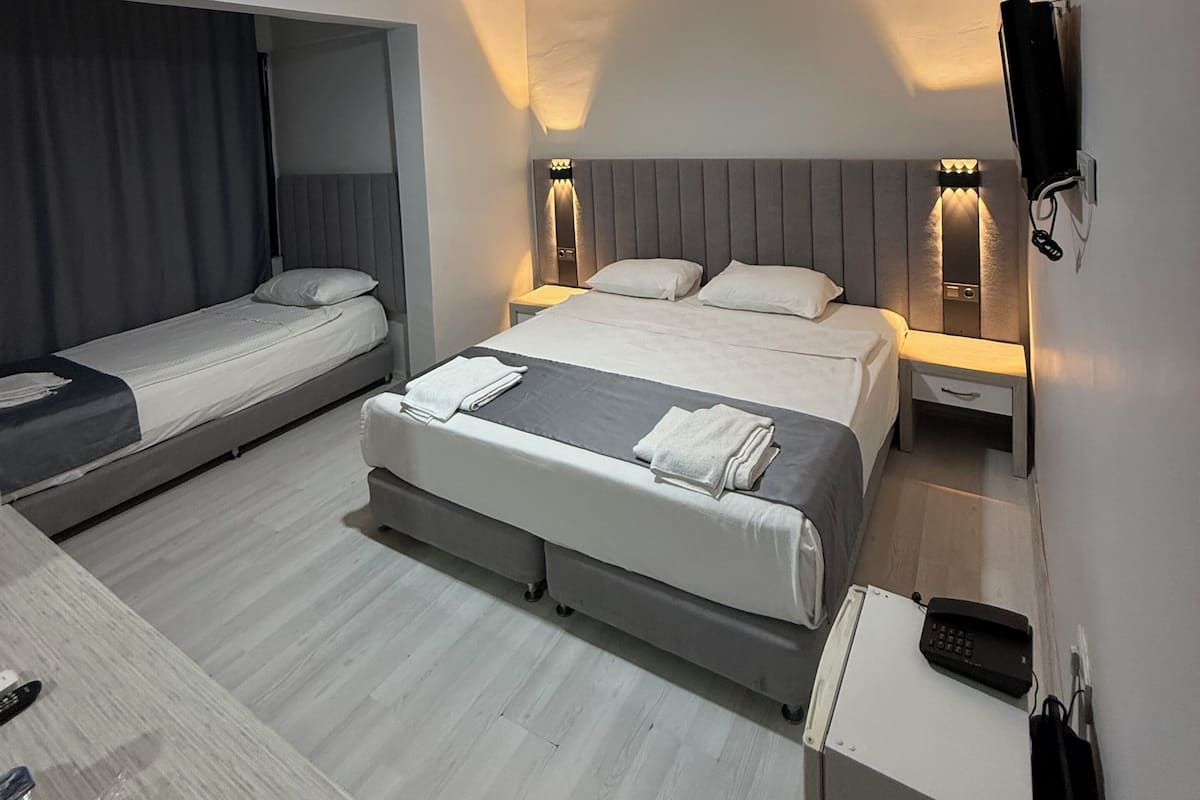 Quarto de hotel com duas camas, uma escrivaninha, uma TV e uma luminária no teto.