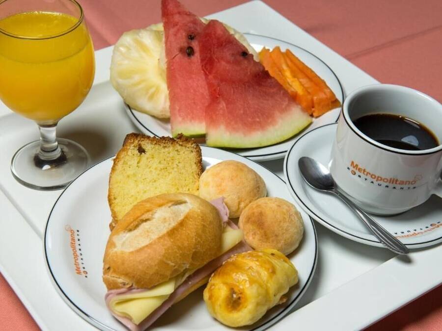 Uma bandeja com alimentos, incluindo pão, sanduíche, croissants, melancia e uma xícara de café.