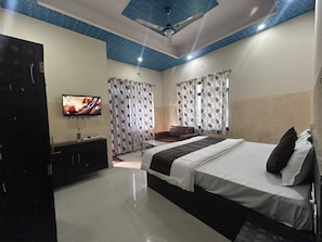 Quarto com cama, televisão, ventilador de teto e cortinas.