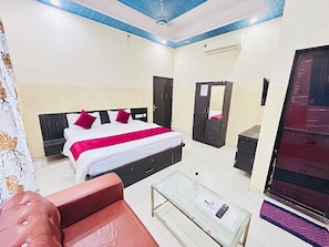 Quarto de hotel com uma cama, uma mesa de centro de vidro, um sofá de couro vermelho, um guarda-roupa e uma porta.