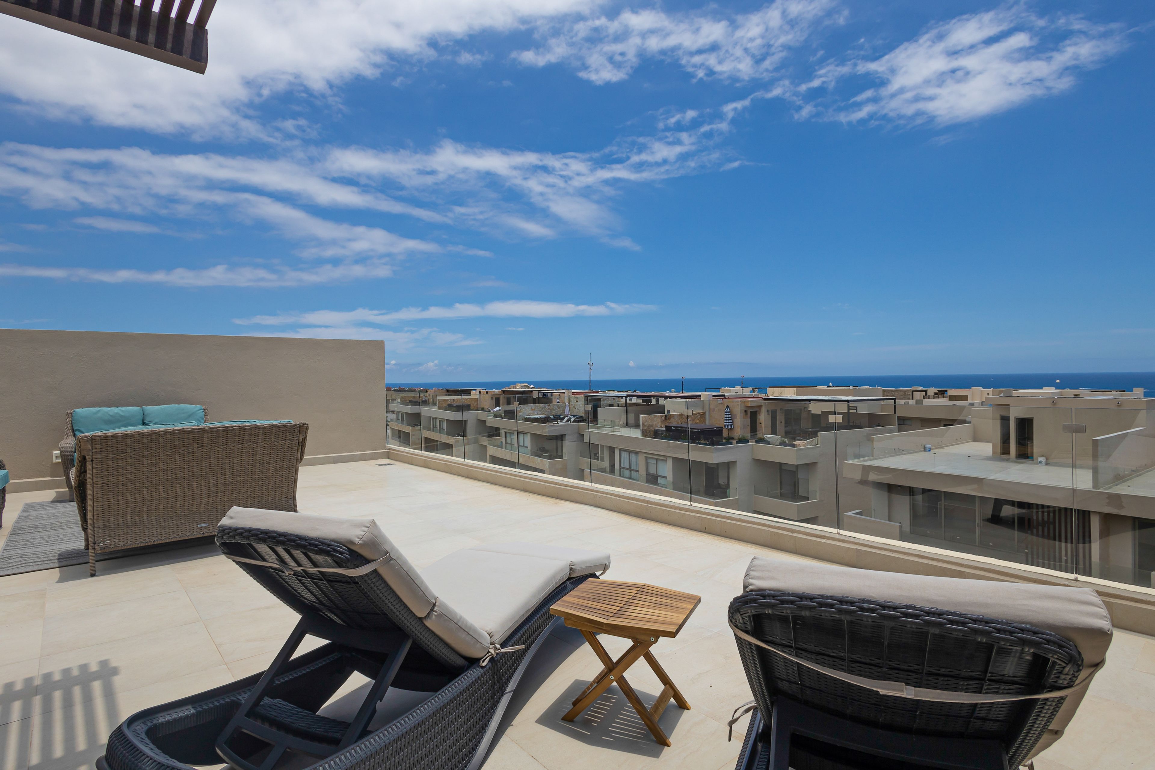 Terraço no telhado com cadeiras de descanso, uma mesinha e vista para a cidade e o oceano.