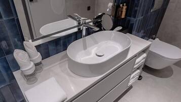 Um banheiro moderno com uma pia oval grande, um espelho, um vaso sanitário e um porta-toalhas.