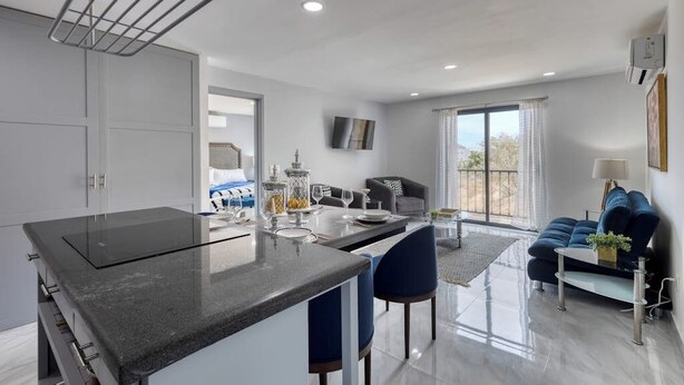 Cozinha moderna com ilha central, área de jantar com sofá e vista para o exterior.