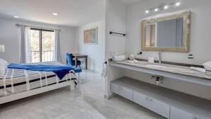 Quarto moderno com cama, escrivaninha, espelho grande e banheiro com toucador.