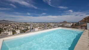 Piscina no terraço com vista para a cidade, céu claro e colinas ao longe.