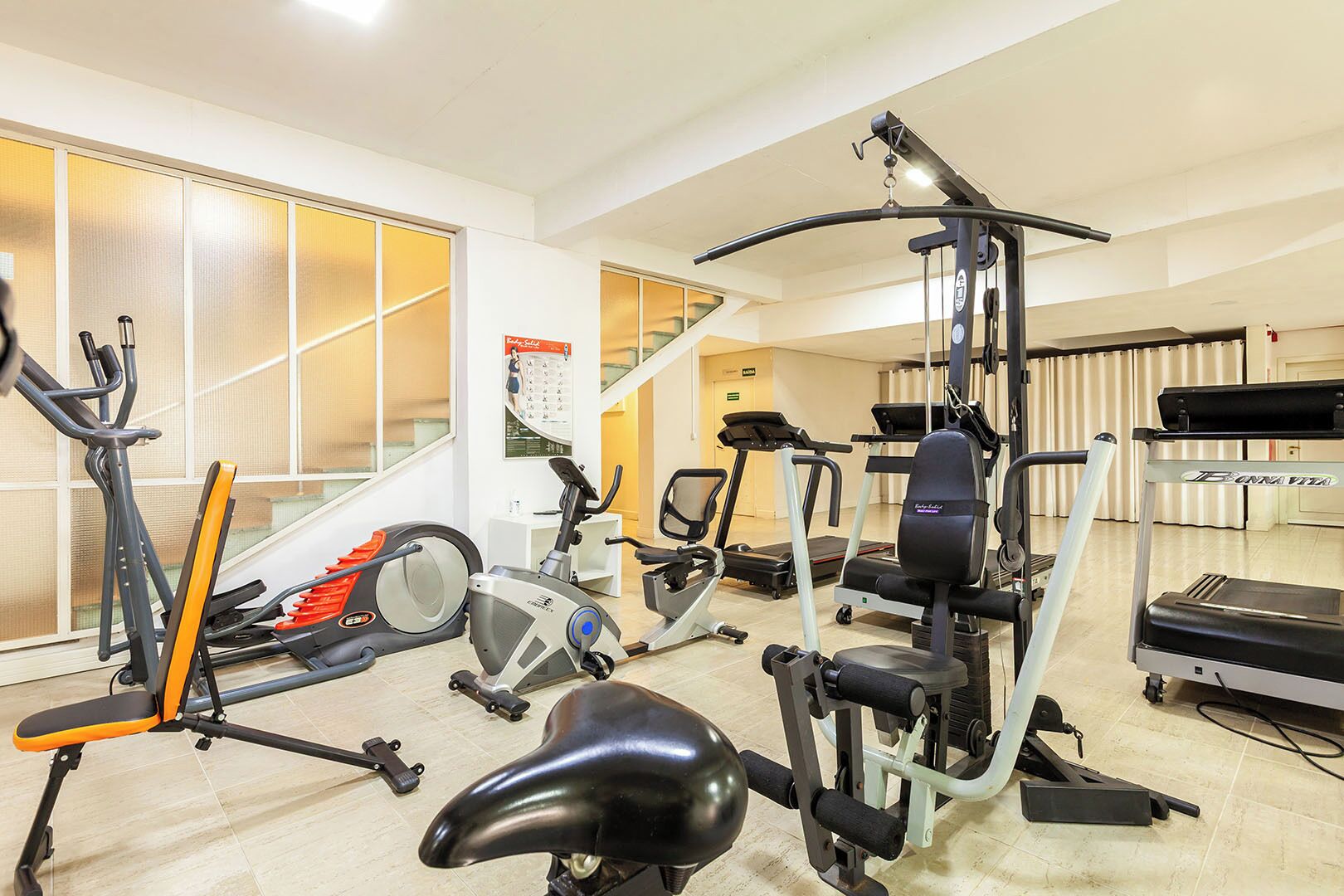 Academia com diversos equipamentos de exercício, esteira e simulador de escada.