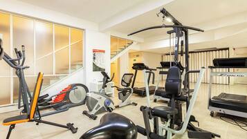 Academia com diversos equipamentos de exercício, esteira e simulador de escada.