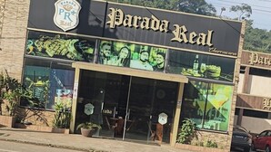 Restaurante chamado 'Parada Real' com uma placa, grandes janelas exibindo comida e bebidas, e um logotipo.
