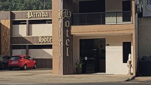 Um hotel com estrutura em dois andares, entrada visível e área de estacionamento com um carro vermelho.