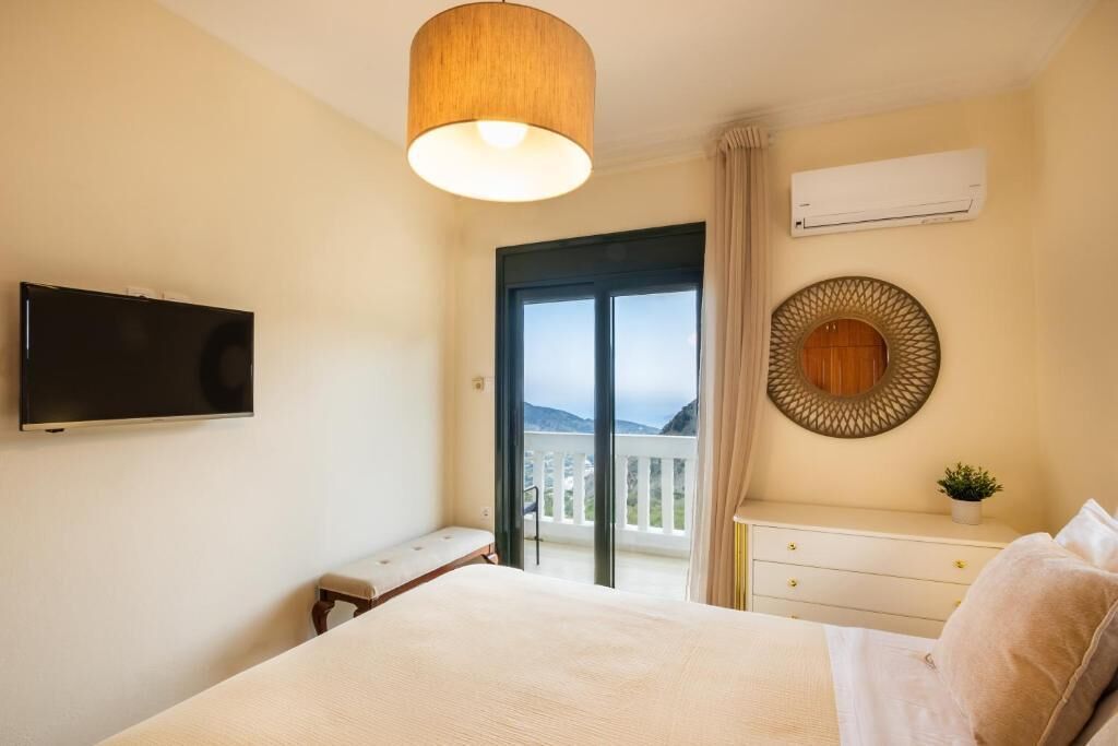 Quarto com cama, televisão, c ômoda, espelho e varanda com vista.
