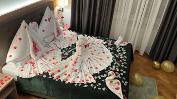 Cama com pétalas de rosa e decorações de cisne, mesa de cabeceira, luminária e vista do quarto.