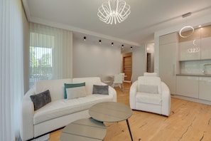 Uma sala de estar moderna com sofá, poltronas, mesa de centro e uma área de cozinha com armários.