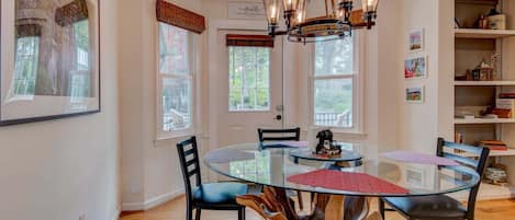 Uma área de refeições com mesa de vidro, cadeiras pretas, um centro de mesa feito com um toco de madeira e um candelabro.