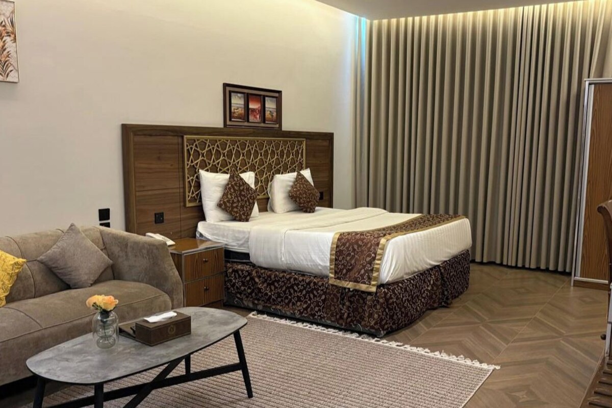 Quarto de hotel com cama, sofá, mesa de centro e guarda-roupa.