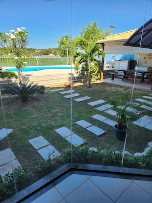 Uma área à beira da piscina com vista clara, um espaço coberto para relaxar e um alpendre com azulejos de pedra e plantas em vasos.