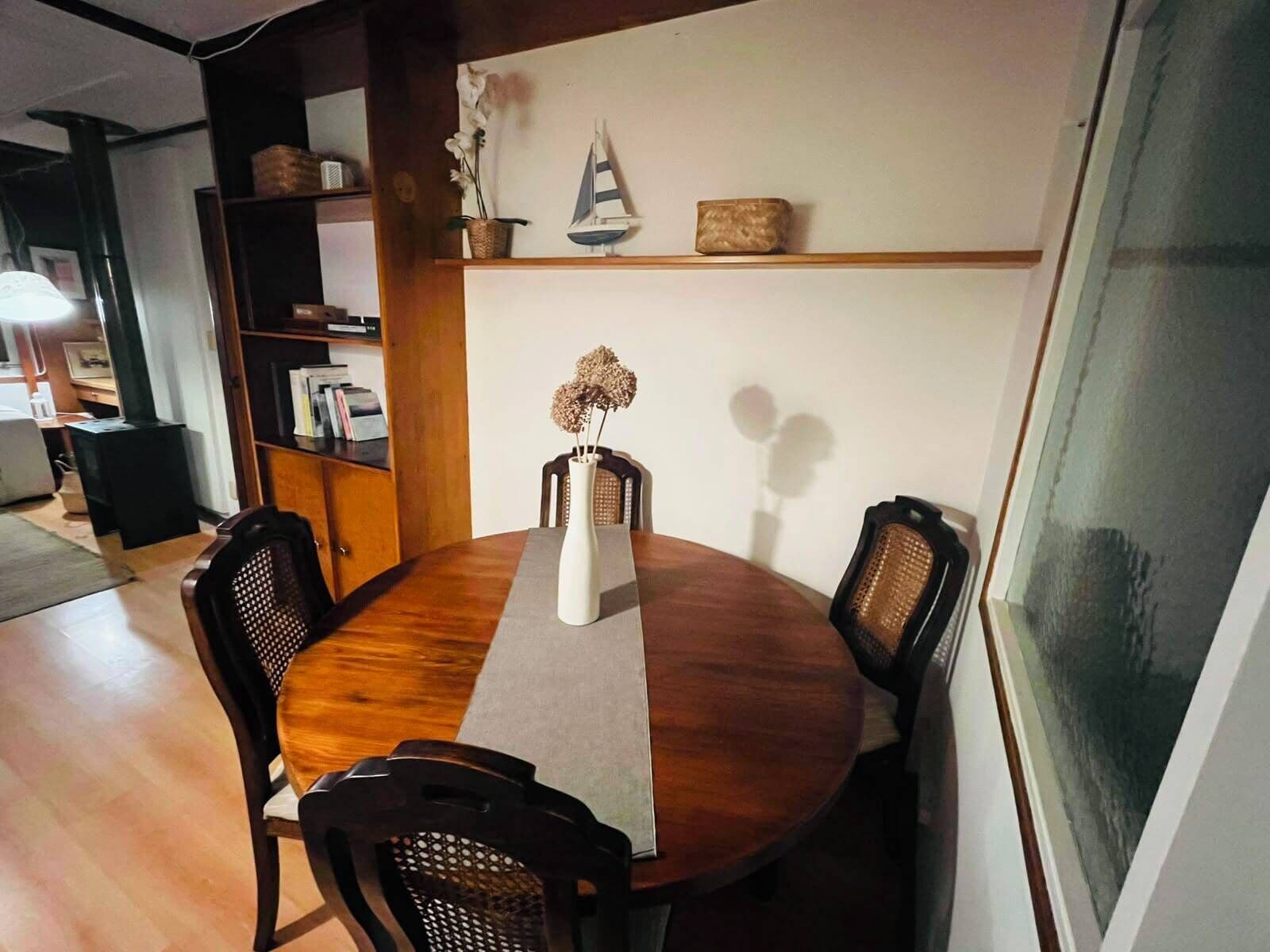Uma mesa de jantar redonda com um vaso de flores secas, rodeada por cadeiras.
