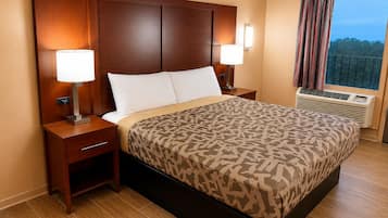 Quarto de hotel com uma cama grande, duas mesas de cabeceira com abajures, uma janela com cortinas e um ar condicionado instalado.