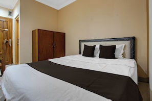 Quarto de hotel com uma cama, um guarda-roupa de madeira e uma porta com puxador.