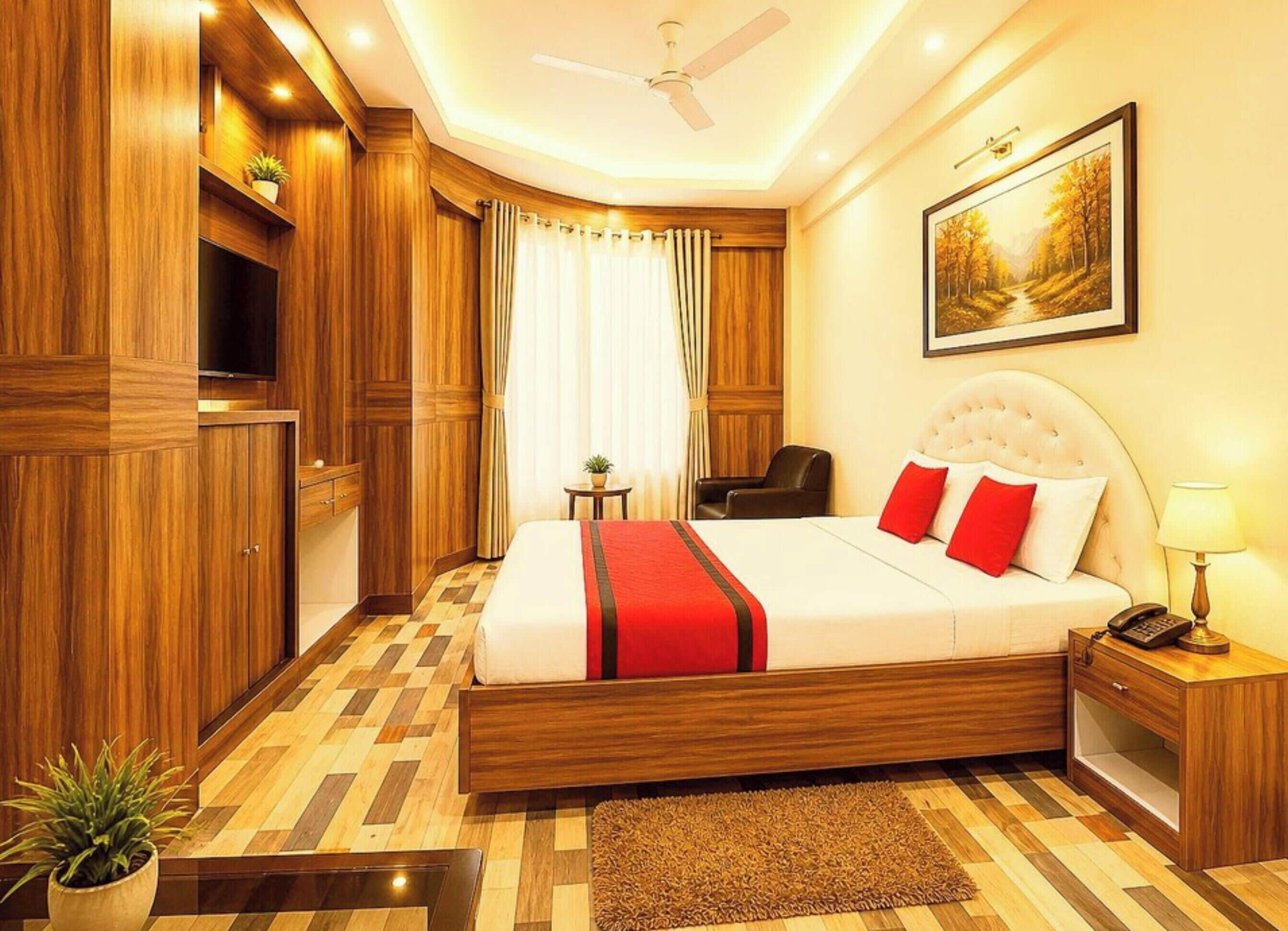 Quarto de hotel com uma cama grande, um ventilador de teto, um quadro na parede e uma pequena mesa com abajur.