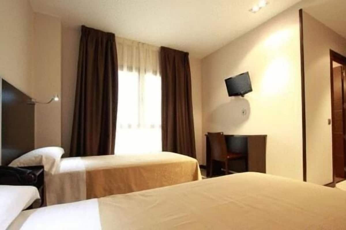 Quarto de hotel com duas camas, televisão na parede e uma mesa.