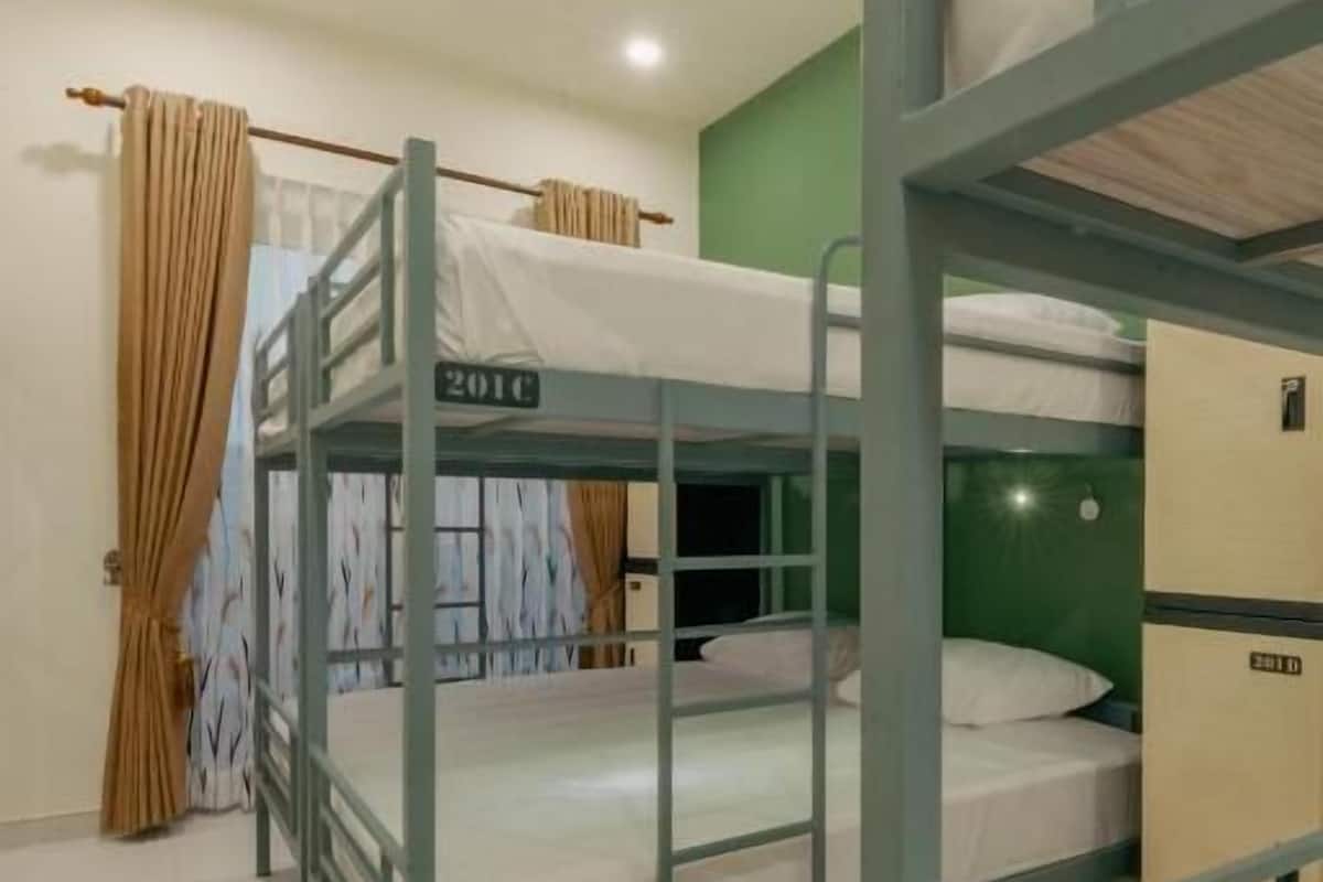 Quarto com beliche, parede verde, janela com cortinas e porta visível.