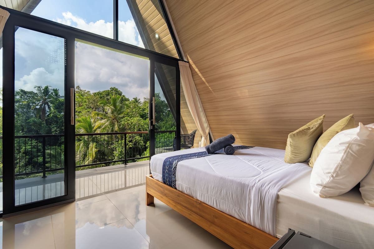 Quarto com uma janela grande, uma cama e vista para o verde.