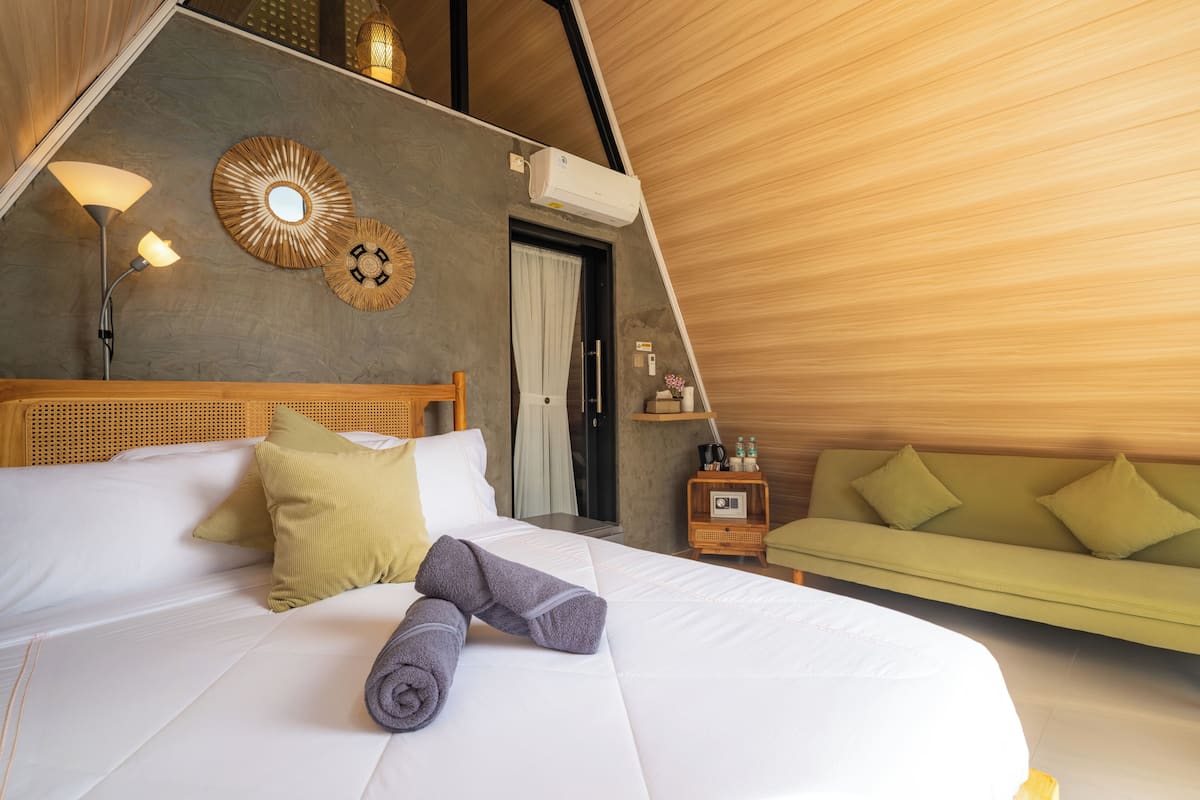 Quarto com uma cama, um sofá verde, ar-condicionado fixado na parede, uma luminária e um espelho decorativo.