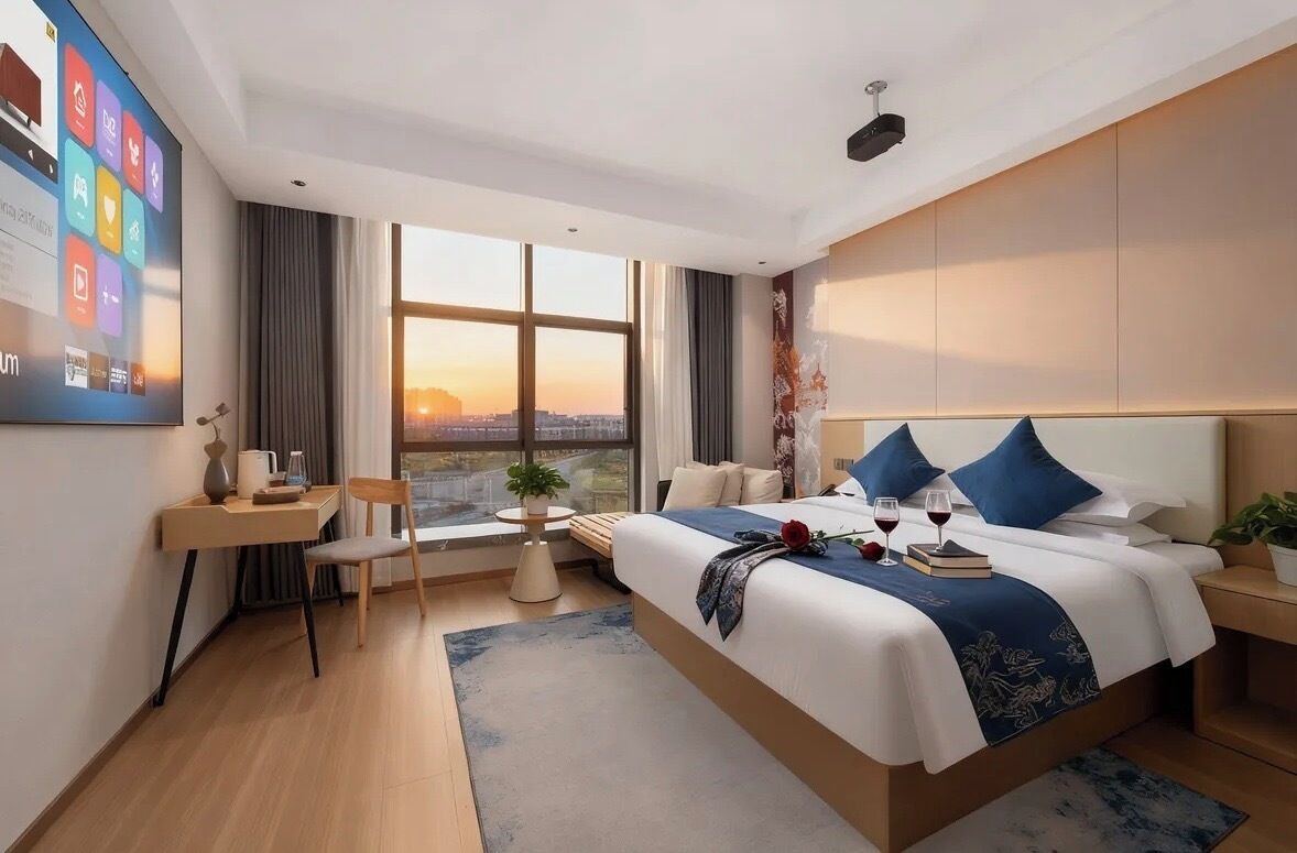 Quarto de hotel moderno com uma cama grande, uma escrivaninha, uma cadeira, uma mesinha de centro com uma planta e uma janela ampla com vista para a cidade.